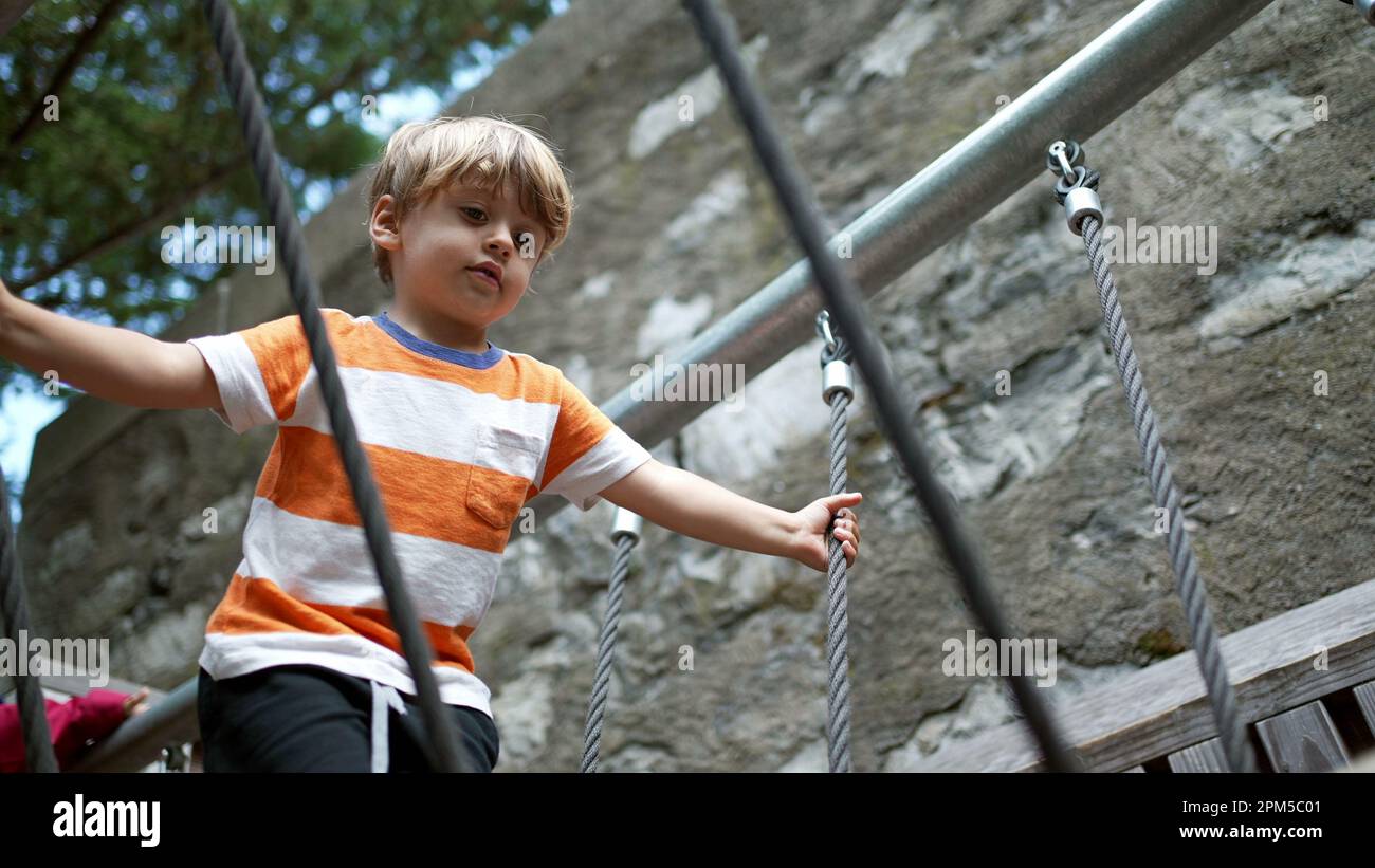Active child staying in balance crossing playground bridge outside. One ...