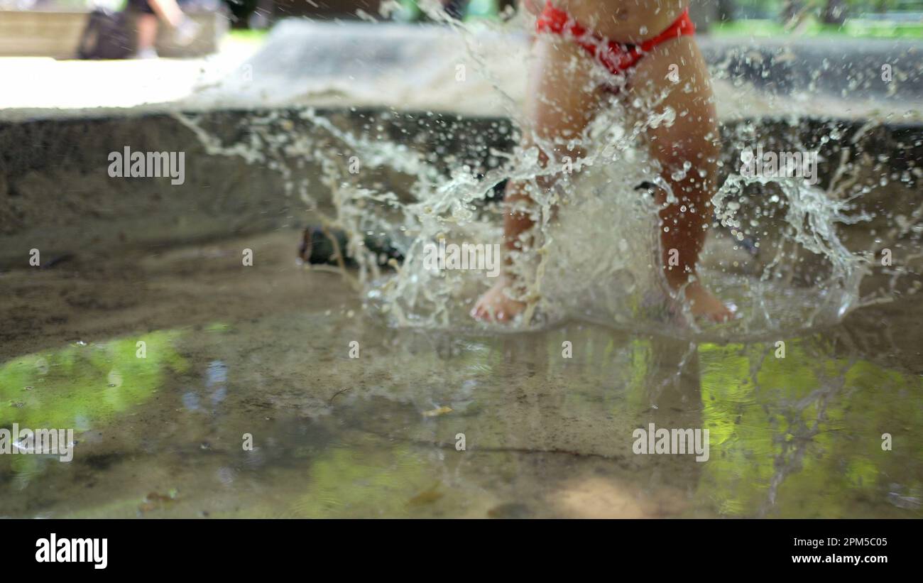 Active child jumping into puddle of water at park during summer day ...
