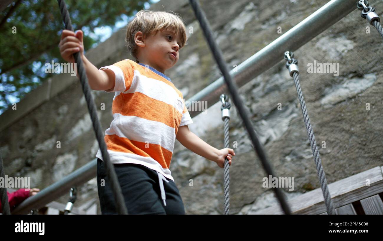 Active child staying in balance crossing playground bridge outside. One ...