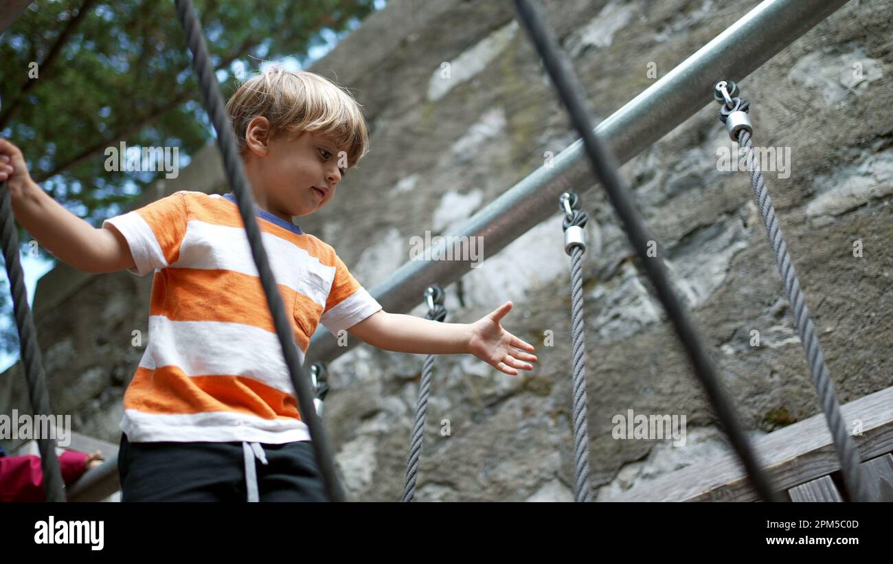 Active child staying in balance crossing playground bridge outside. One ...