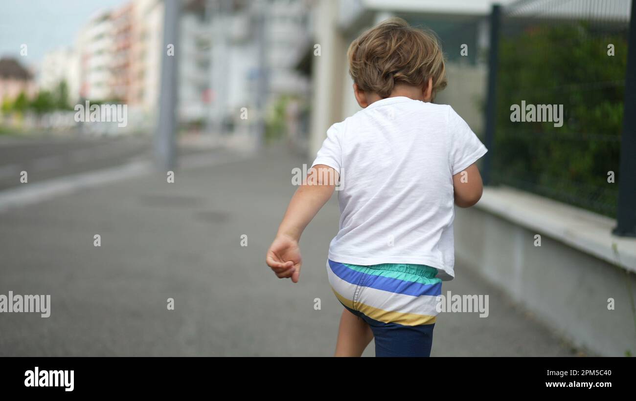 Back of happy kid walking outside in city street. Child standing in ...