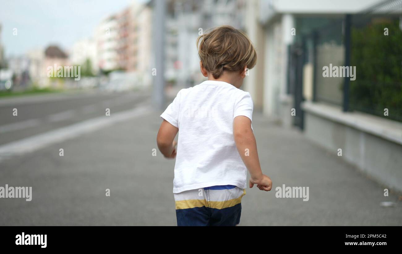Back of happy kid walking outside in city street. Child standing in ...