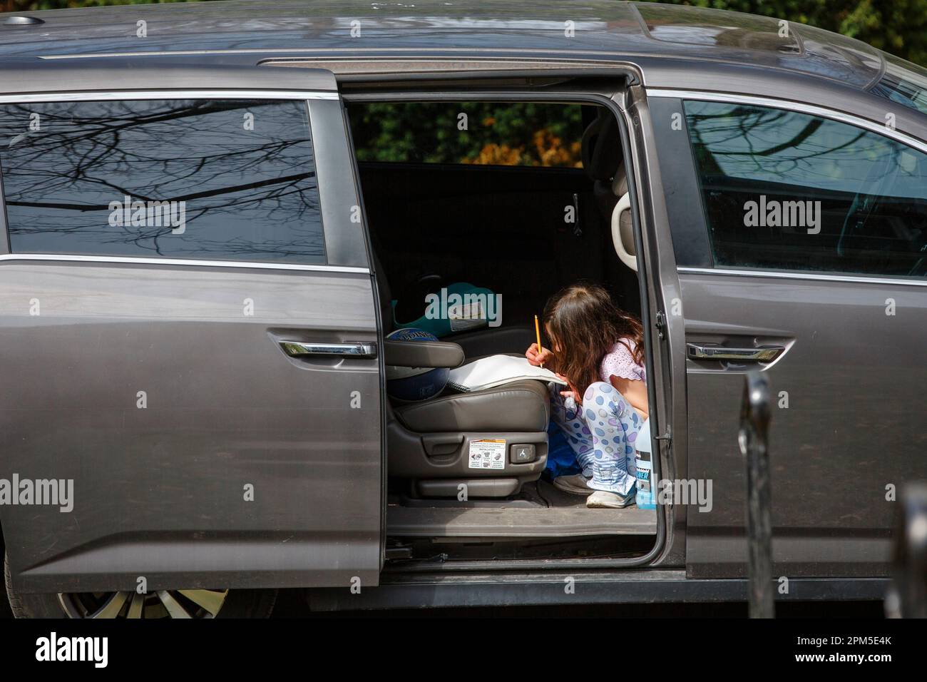 A small child sits in open van drawing with pencil and paper Stock ...
