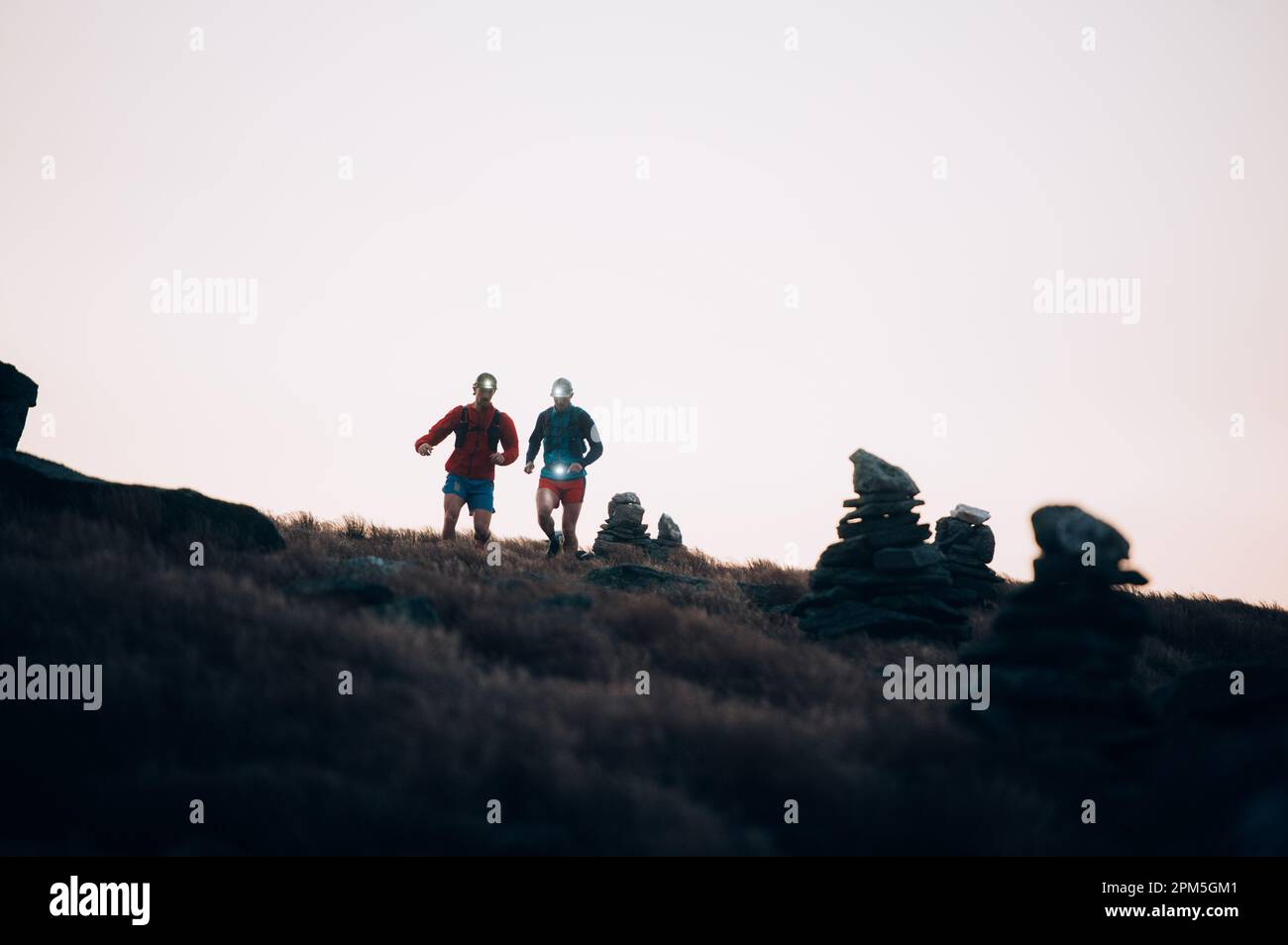 Male trail runners running through grass and cairns at dawn Stock Photo ...
