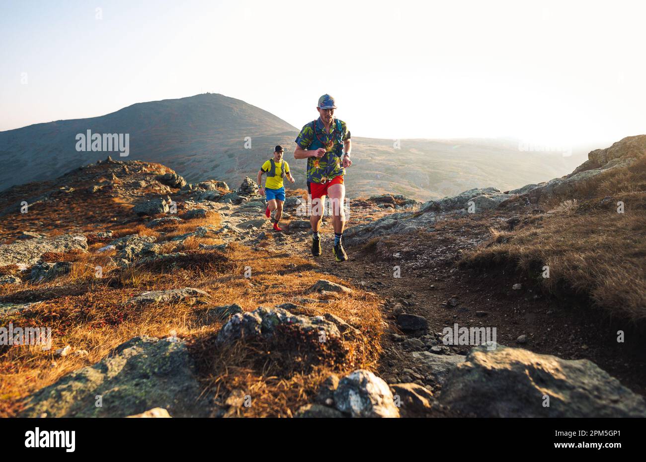Male trail runners running along trail at sunrise in mountains Stock ...
