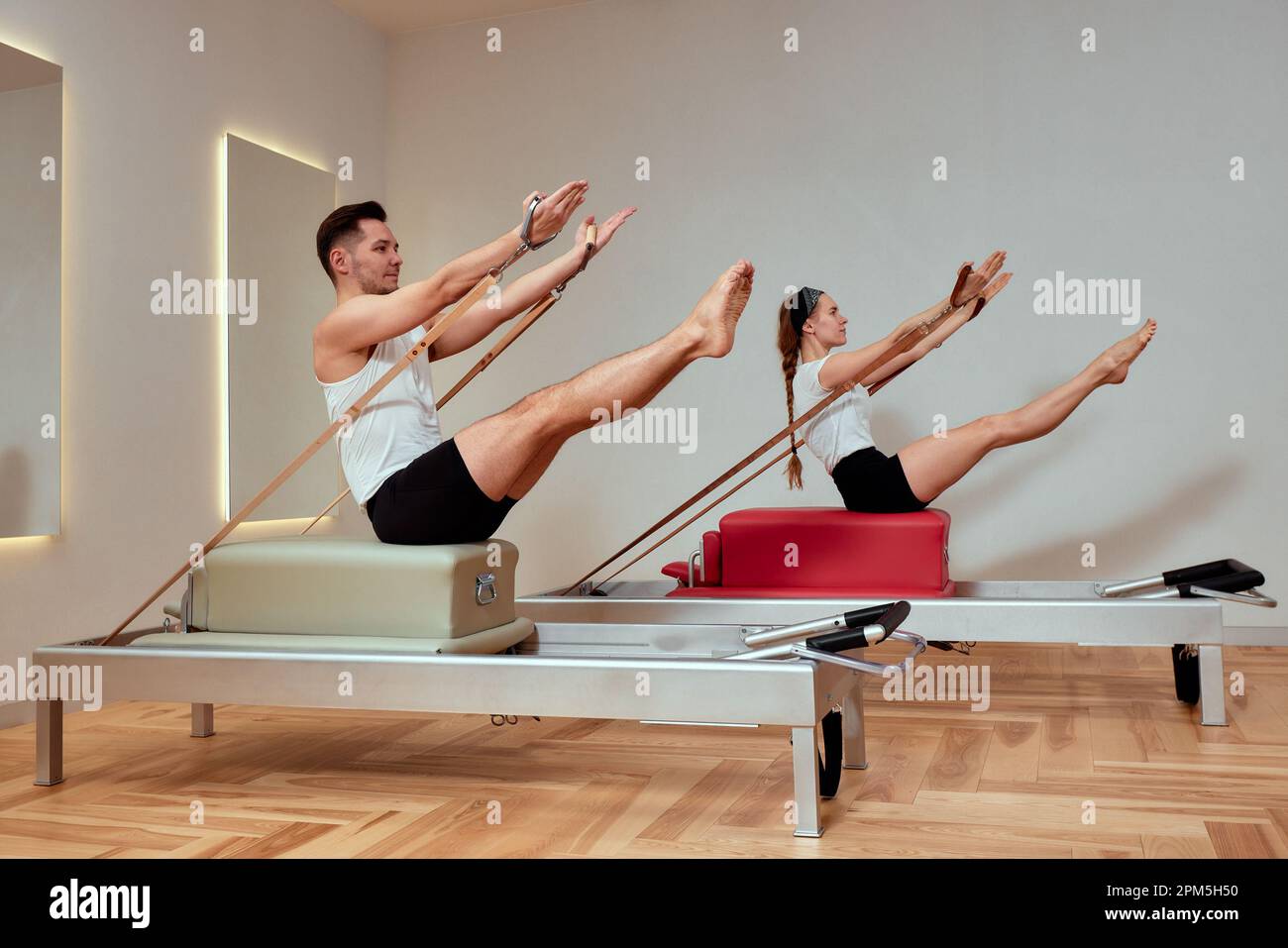 A man and a woman in a pair do pilates exercises on reformers ...