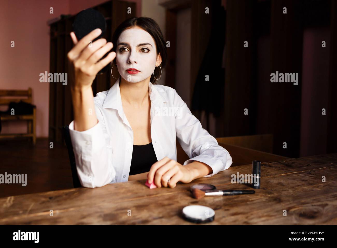 actress applies makeup to her face while sitting at rehearsal theater ...