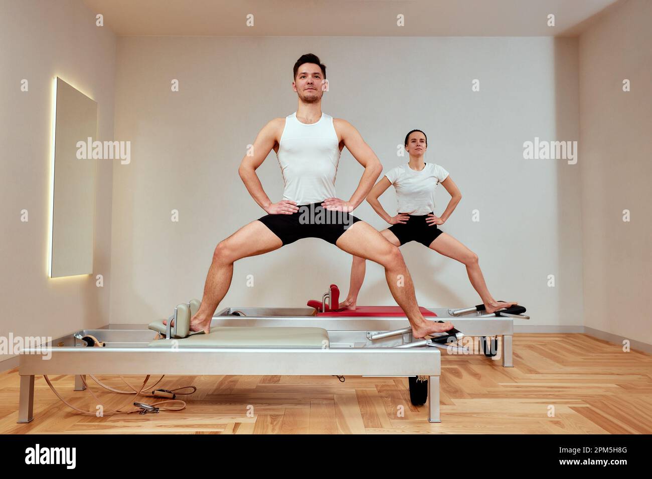 A man and a woman in a pair do pilates exercises on reformers ...