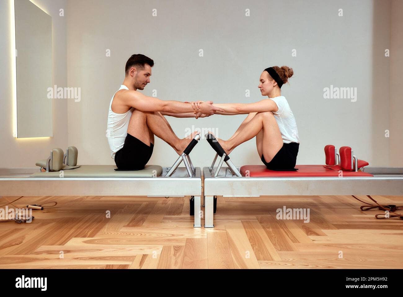 A man and a woman in a pair do pilates exercises on reformers ...