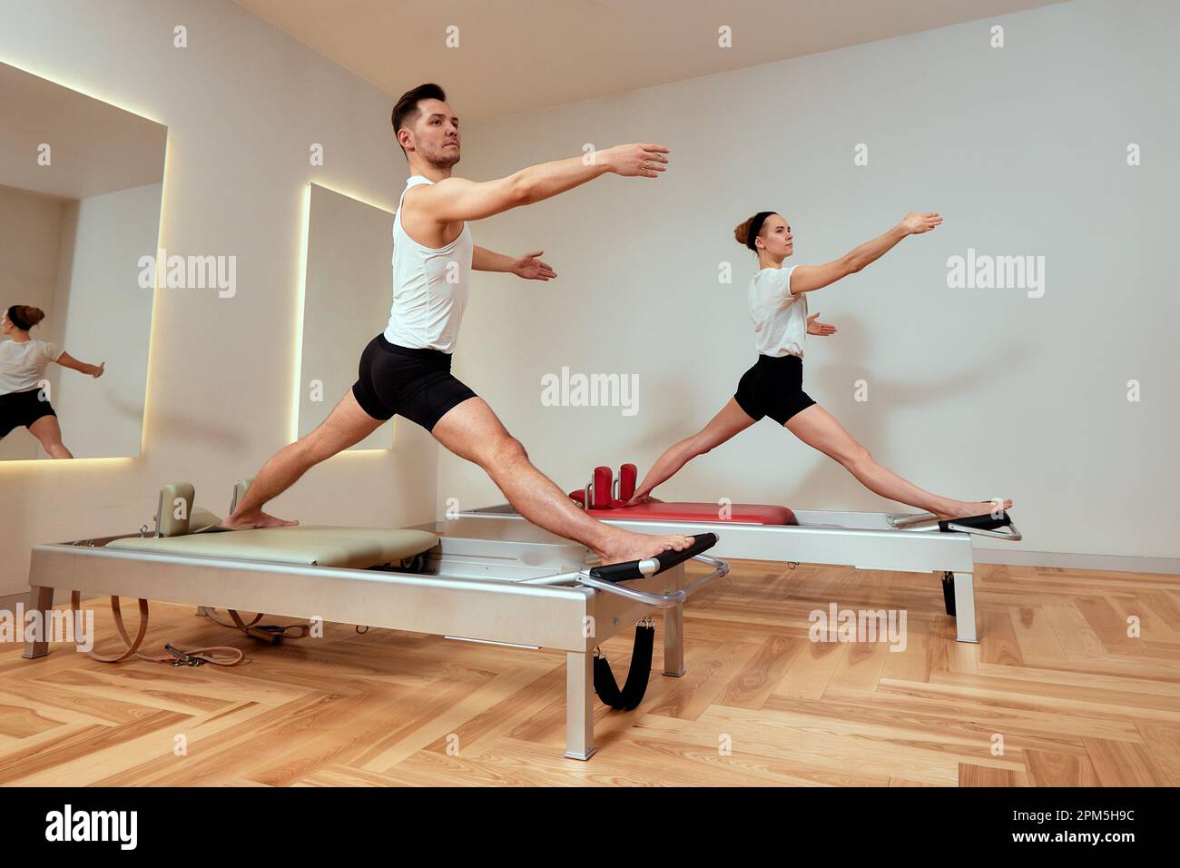 A man and a woman in a pair do pilates exercises on reformers ...