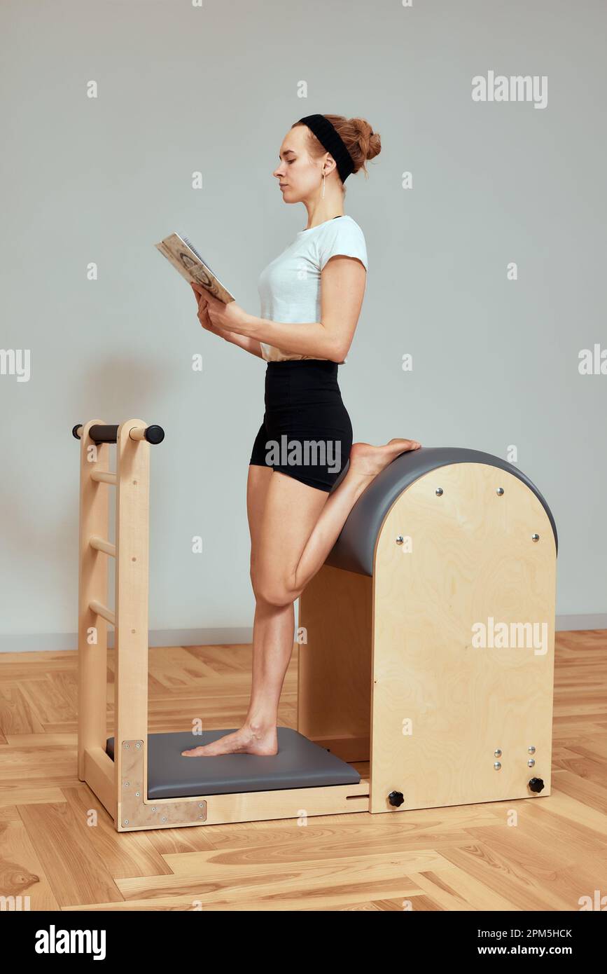 woman doing pilates exercises on reformer, woman reading a book during ...