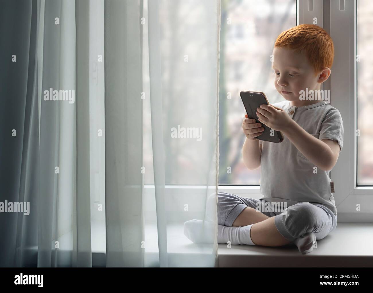 The child watches cartoons on the phone while sitting on the window ...