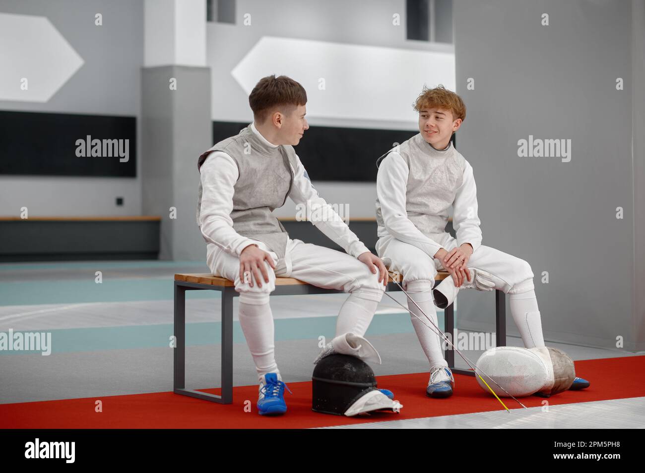 Two young fencers talking while sitting on bench after training Stock ...