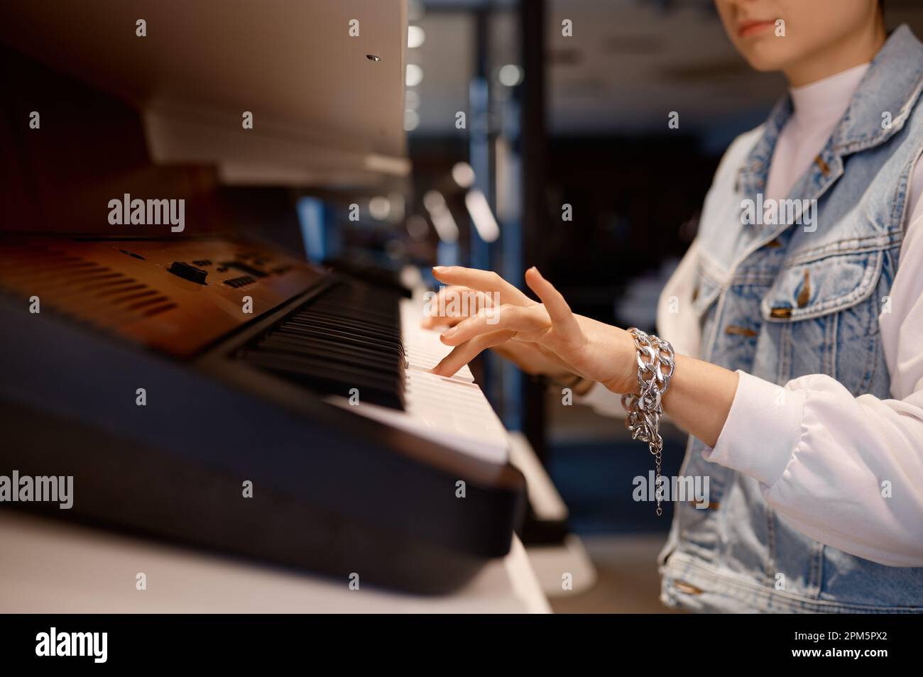 Young female hipster playing eclectic piano keyboard at musical shop ...