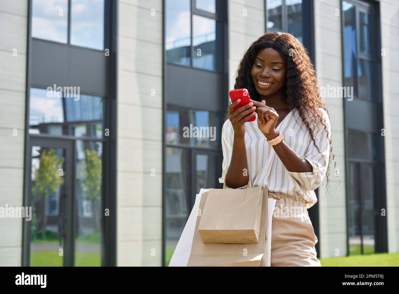 Happy black woman shopper standing on street holding shopping bags and ...