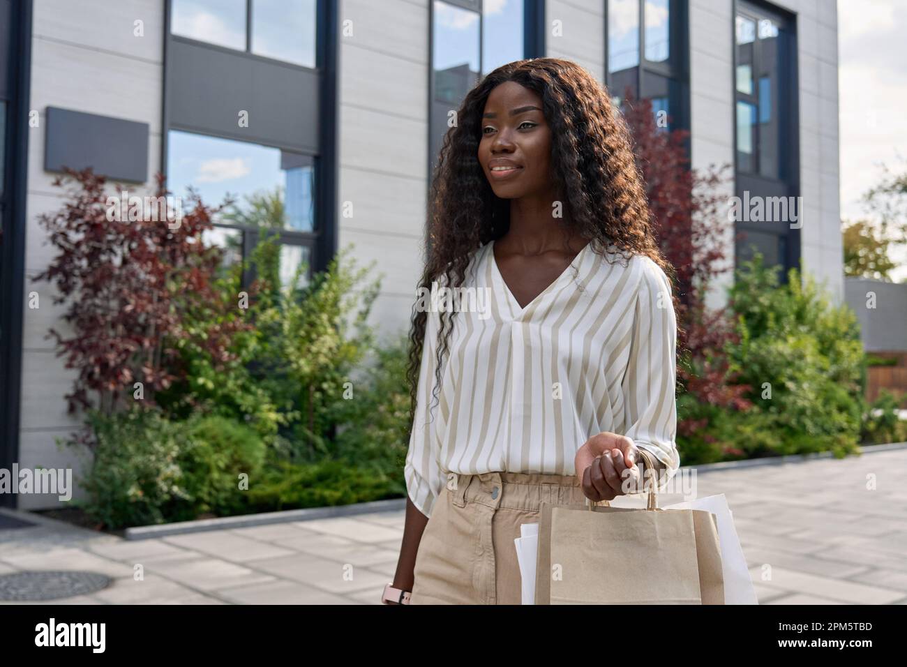 Young black woman shopper walking on city street holding shopping bags ...