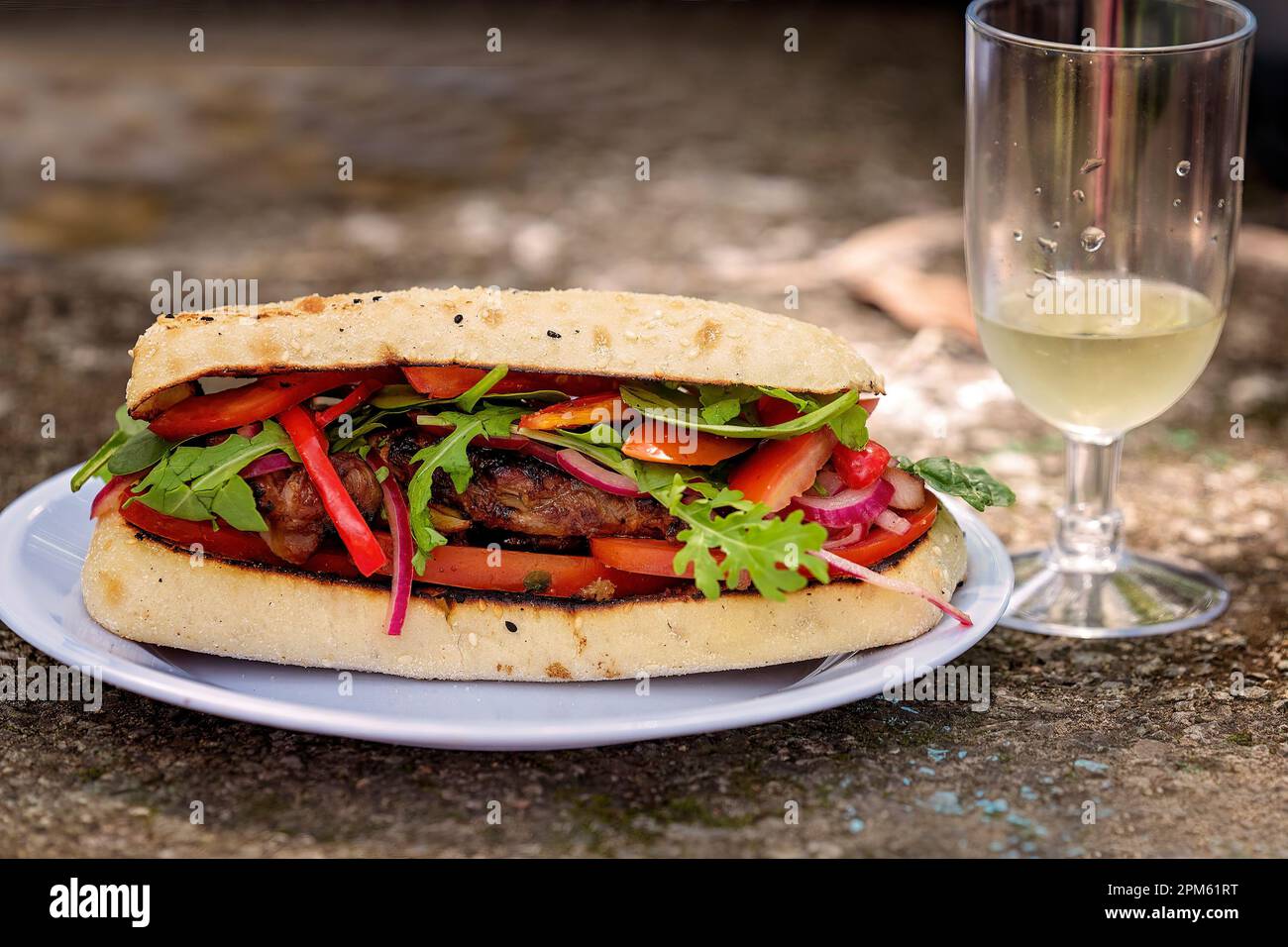 An outdoor bush barbecue meal of a steak and salad roll and a glass of ...