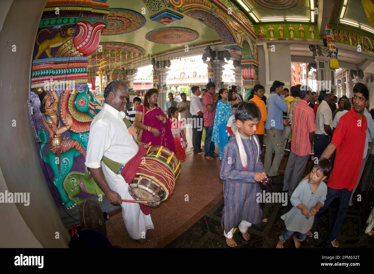 Musician banging drum by gaudy painted column during Deepavali ceremony ...