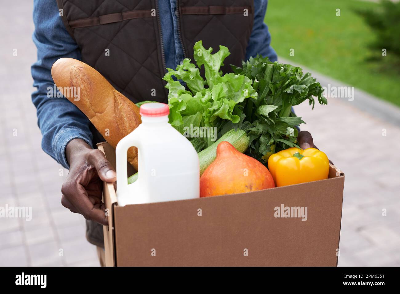 Closeup of black young man carrying box with fresh vegetables while ...