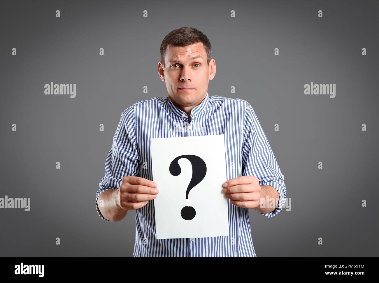 Emotional man holding paper with question mark on grey background Stock ...