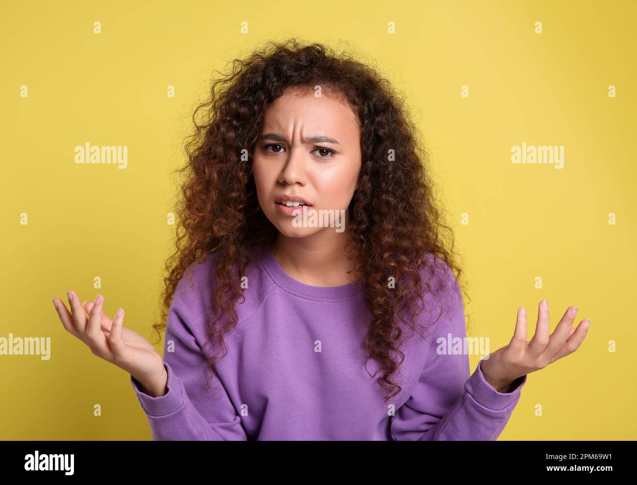 Confused African-American woman on yellow background. Thinking about ...