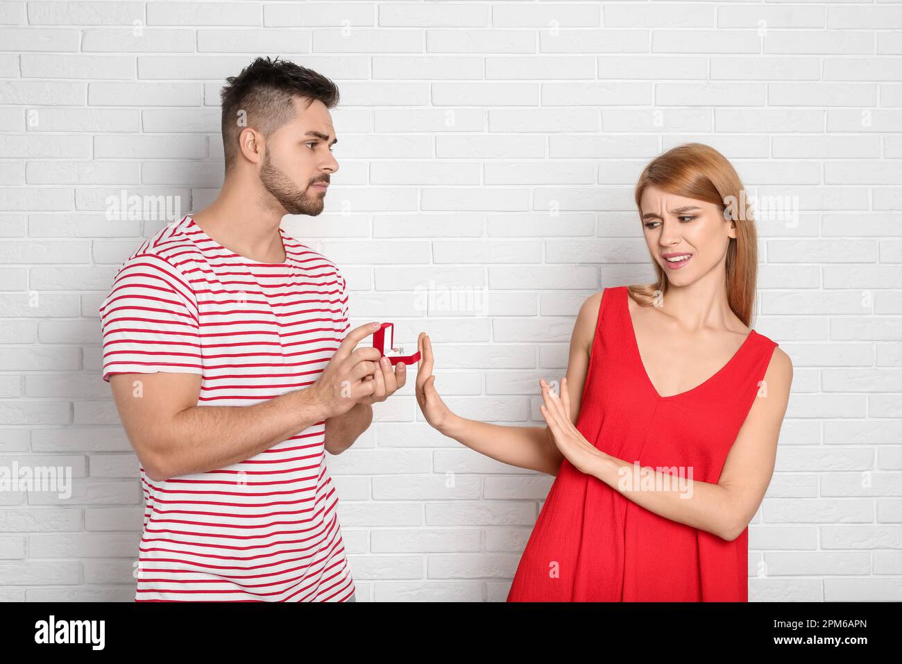 Young woman rejecting engagement ring from boyfriend near white brick ...