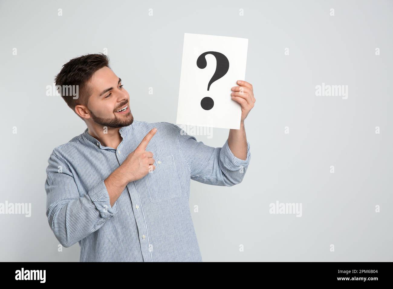 Happy man holding question mark sign on light background Stock Photo ...