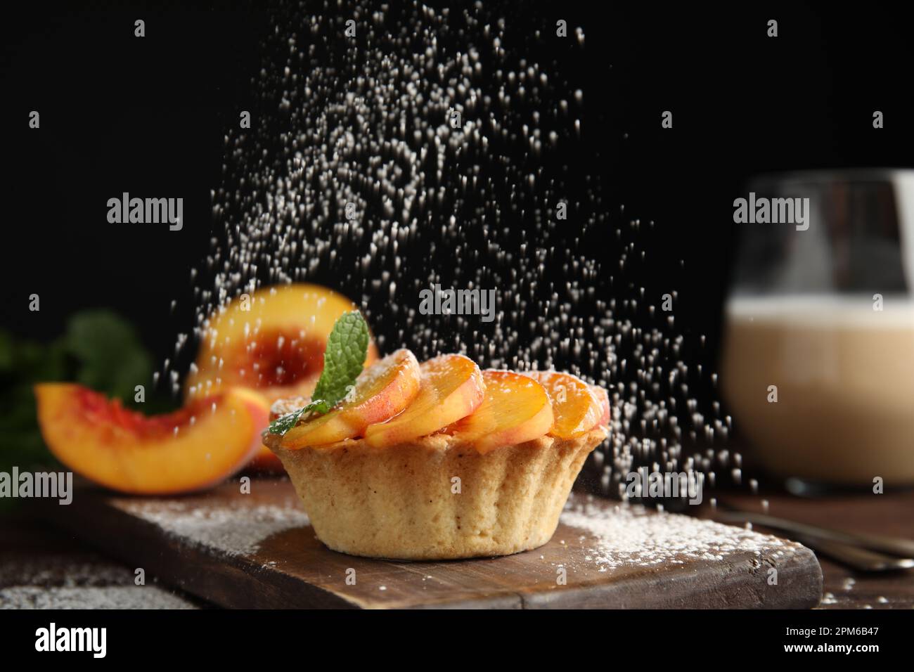 Decorating delicious peach dessert with powdered sugar on wooden board ...