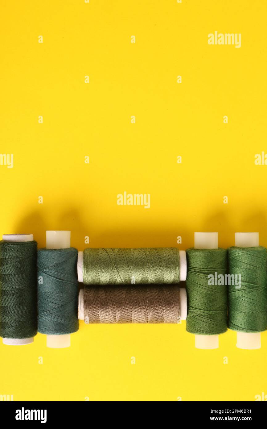 Different shades of green sewing threads on yellow background, flat lay ...