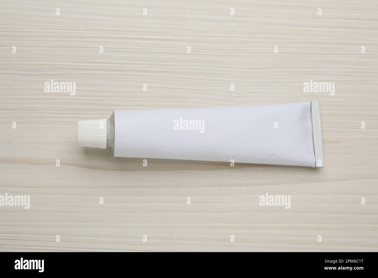 Blank white tube of ointment on light wooden table, top view. Space for ...
