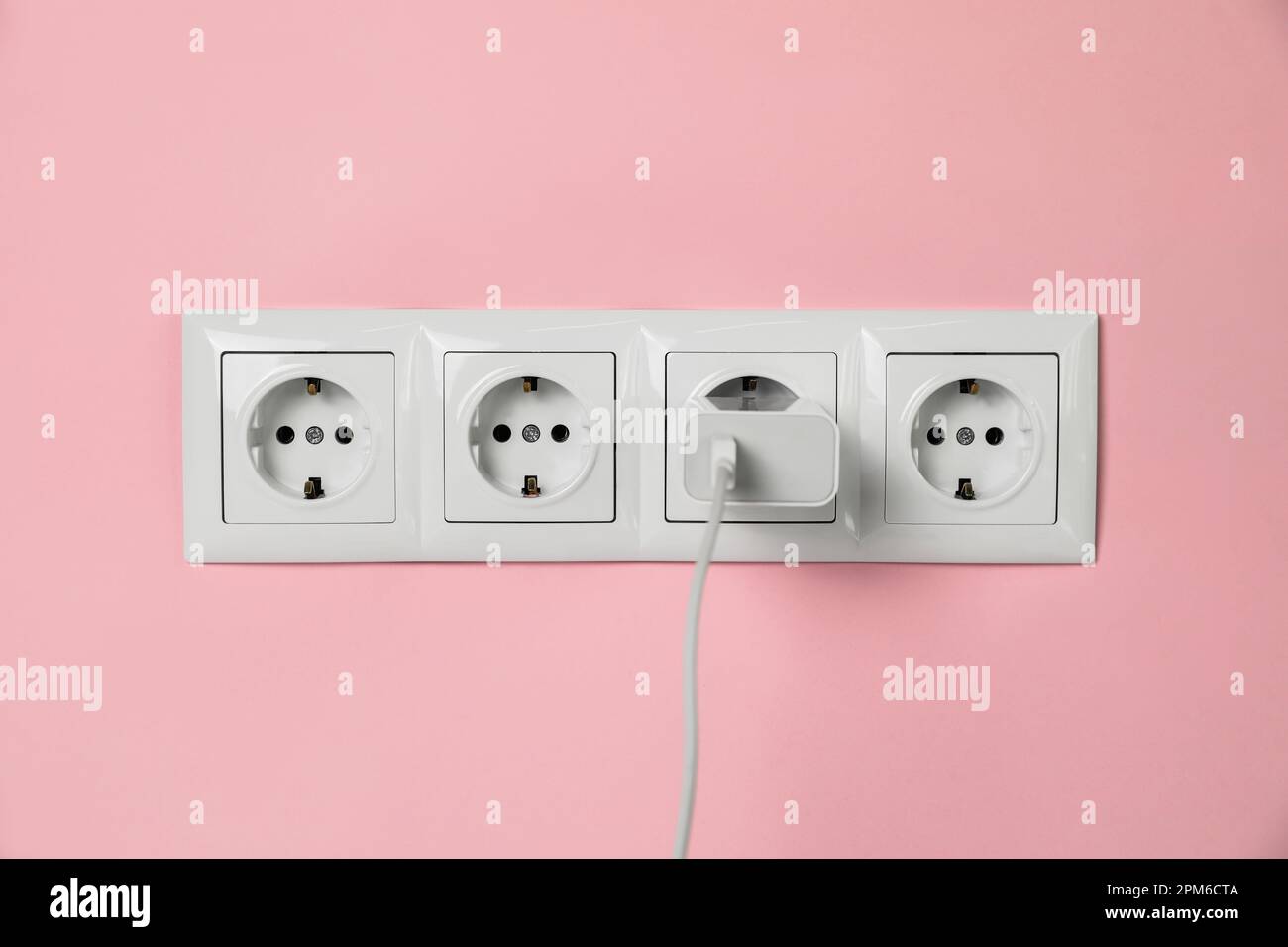 Charger adapter plugged into power sockets on pink wall. Electrical ...