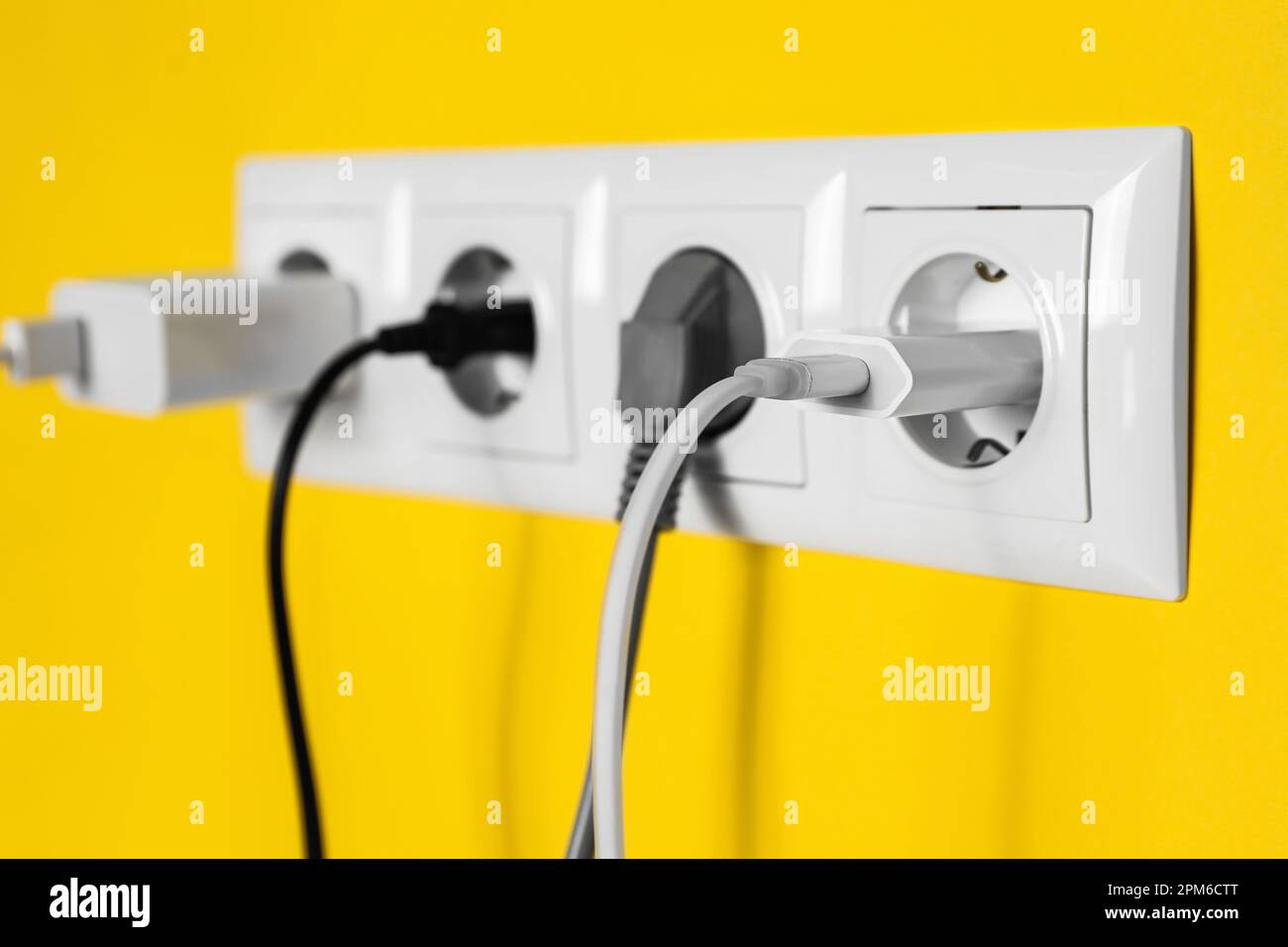 Power sockets with inserted plugs on yellow wall, closeup. Electrical ...