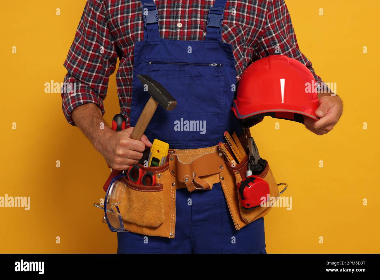 Professional builder in uniform with hammer and tool belt on yellow ...