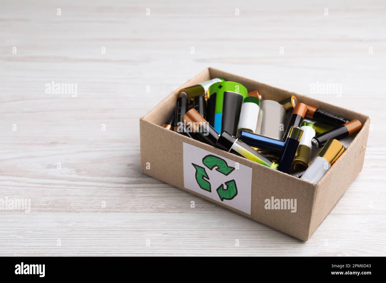 Used batteries in cardboard box with recycling symbol on white wooden ...