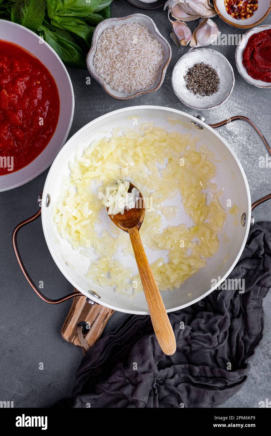 Diced onions being cooked in a white pot, chopped tomatoes, rice ...