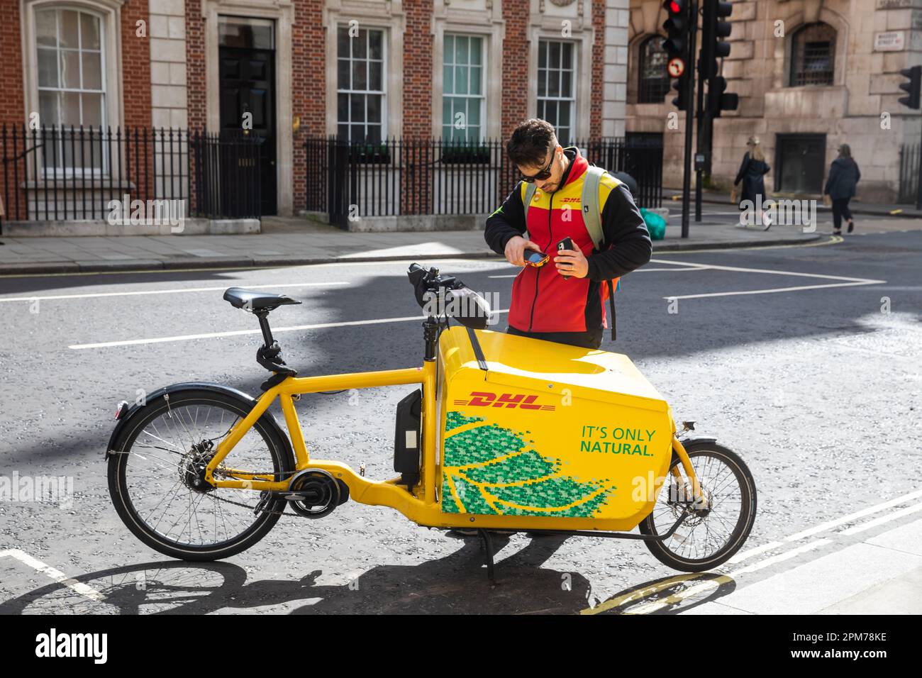 DHL delivery driver on a bicycle scans a parcel in central London Stock ...