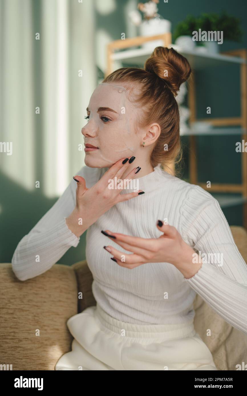 Woman applying white sheet facial mask on face in the modern living ...