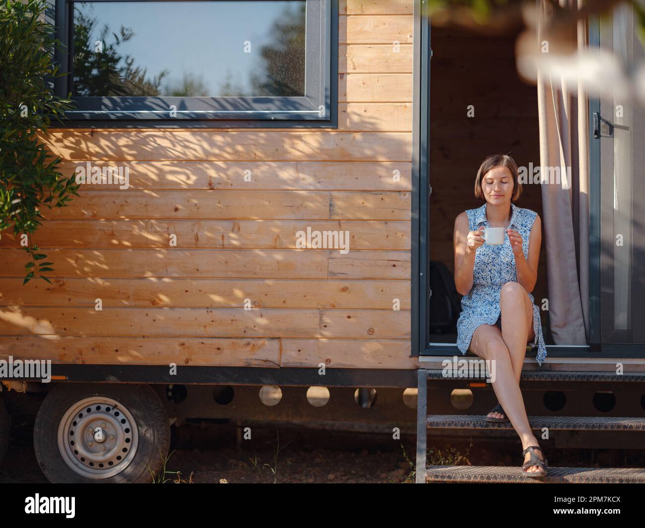 Woman is drinking coffee , morning routine near her Tiny house. First ...