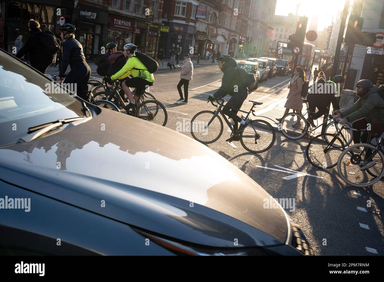 Cyclists make their ways home past a car bonnet in evening sunshine at ...