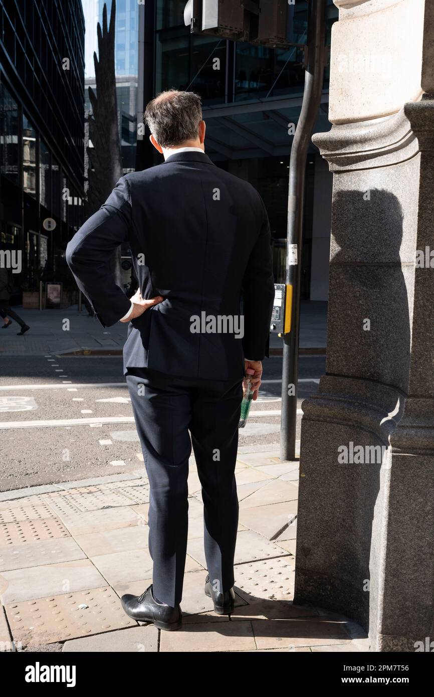 A rear view of a businessman standing on his own at a street corner in ...