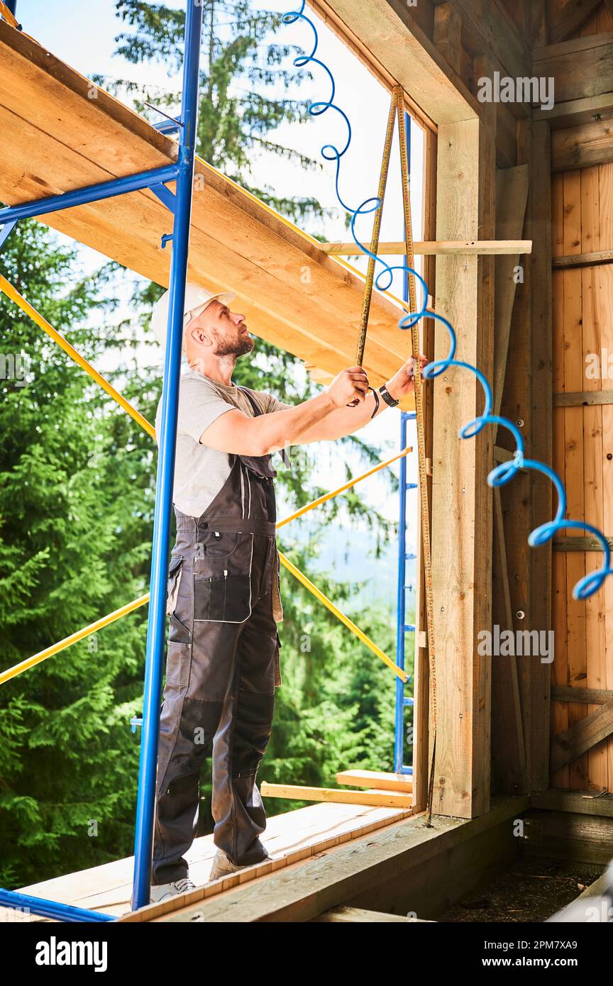 Carpenter building wooden frame house. Man measures distance with tape ...