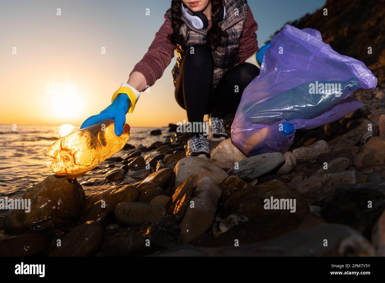 A female volunteer picks up garbage on the ocean. Cleaning of the ...