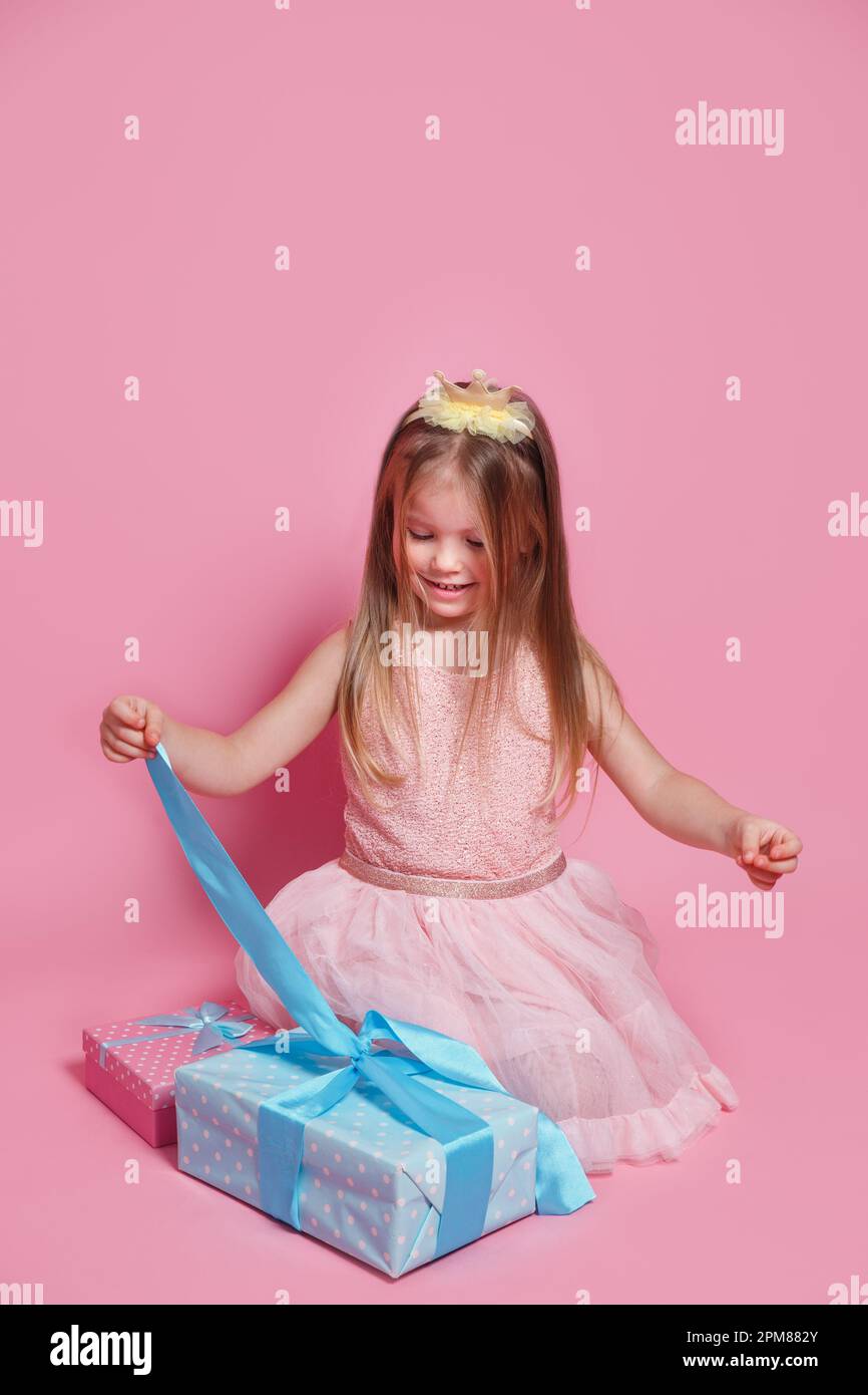 Cute excited kid girl opening present box sitting on pink studio ...