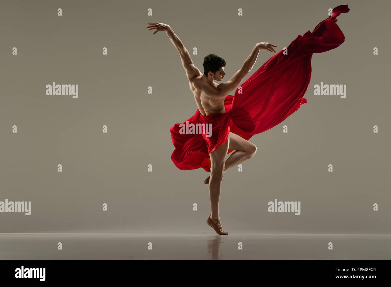 Young, handsome, muscular man dancing with red silk fabric against grey ...
