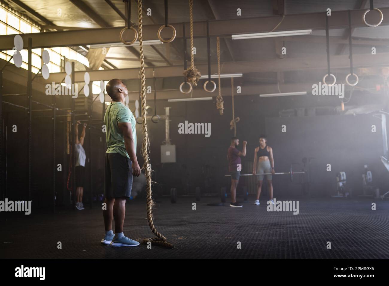 Side view of biracial young man looking at rope while standing in gym ...