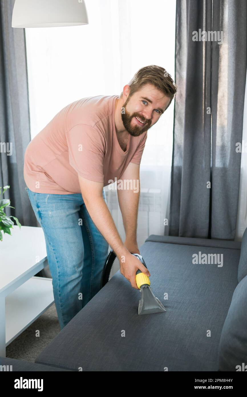 Man holding modern washing vacuum cleaner and cleaning dirty sofa with professionally detergent ...