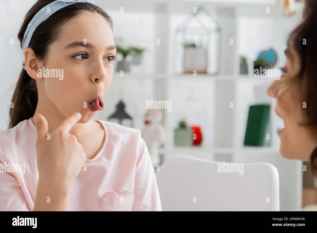 Preteen kid pointing at tongue near blurred speech therapist in consulting room,stock image ...