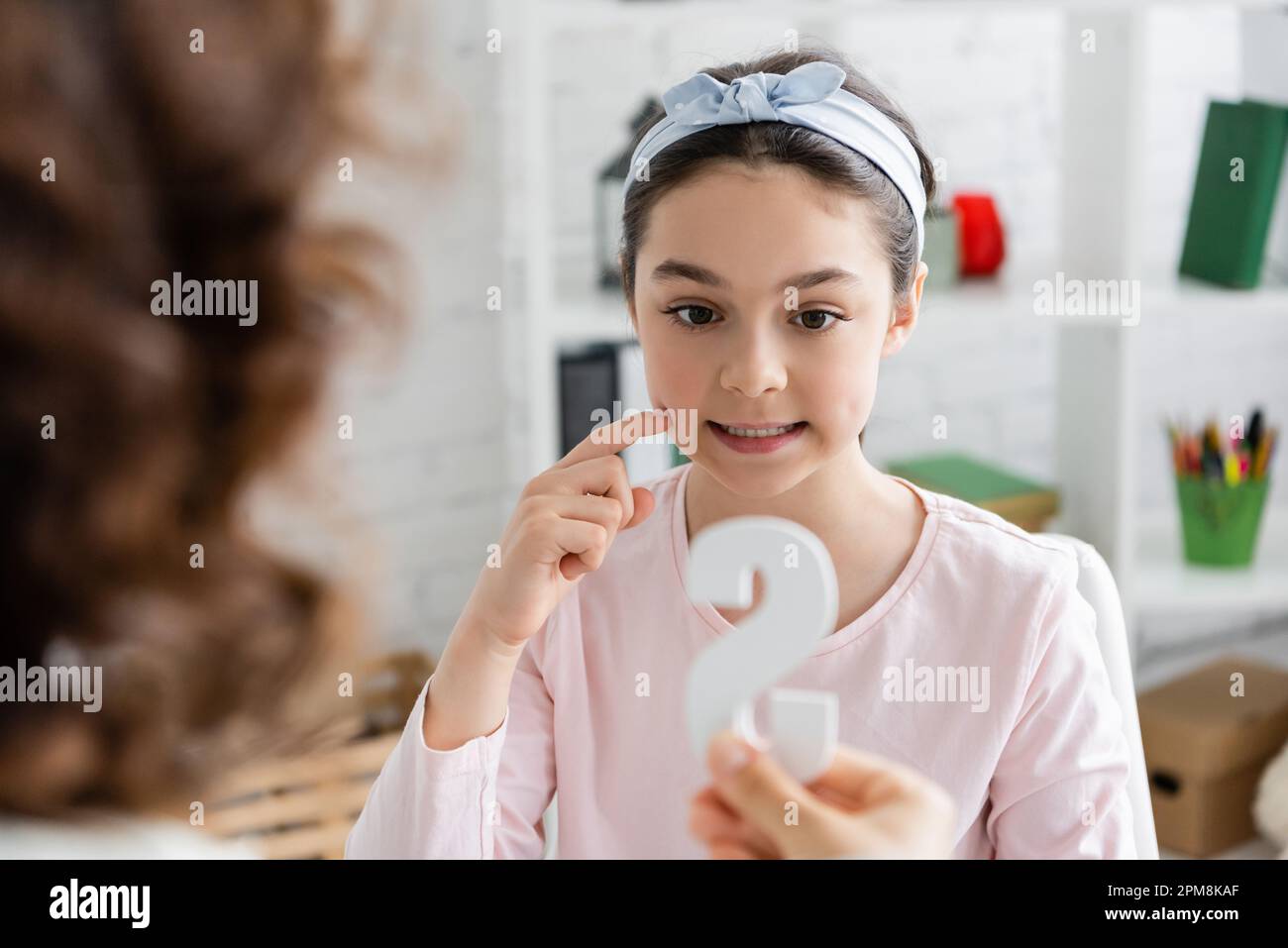 Preteen pupil touching cheek and holding blurred letter s near speech ...
