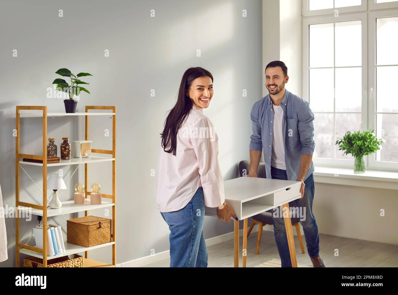 Happy young family couple moving furniture and putting a new desk in ...