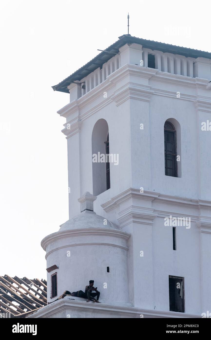 Old Goa, India - January 2023: Two men sitting on a ledge on the roof ...